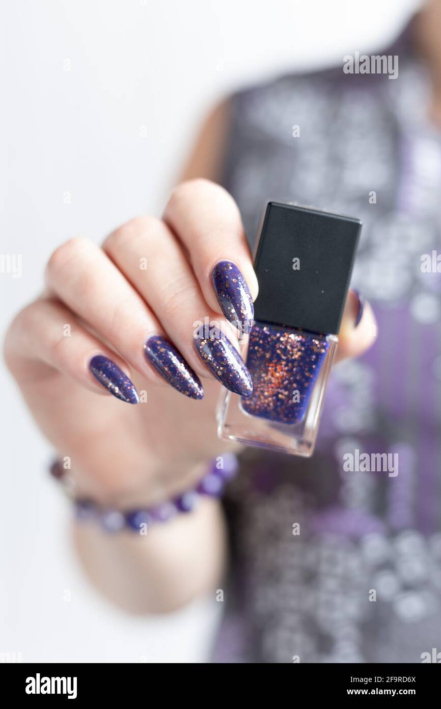 Female hand with long nails and purple lilac manicure holds a bottle of ...
