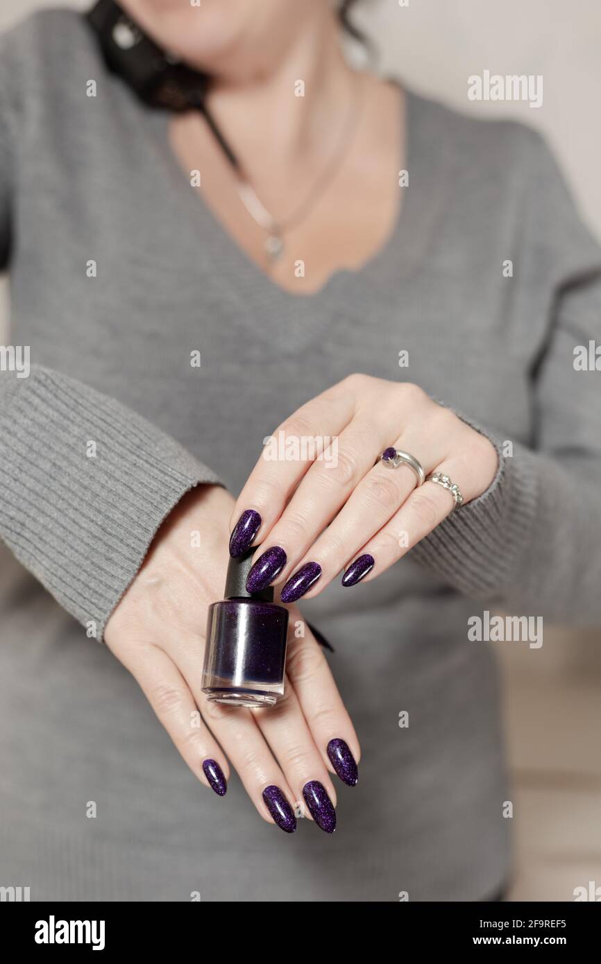Female hand with long nails and dark purple lilac manicure holds a ...