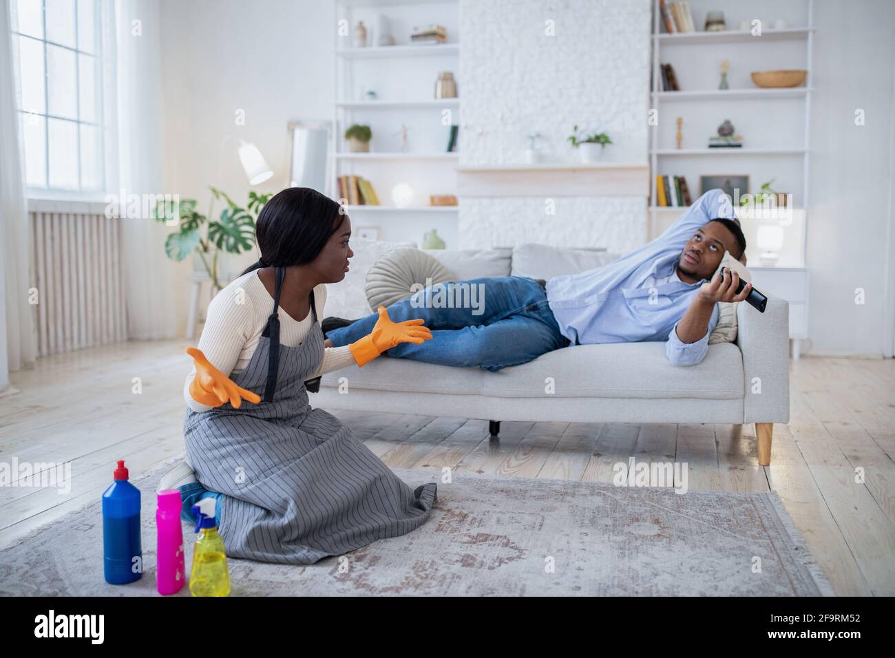 Young black woman sitting on floor, cleaning apartment, arguing with ...