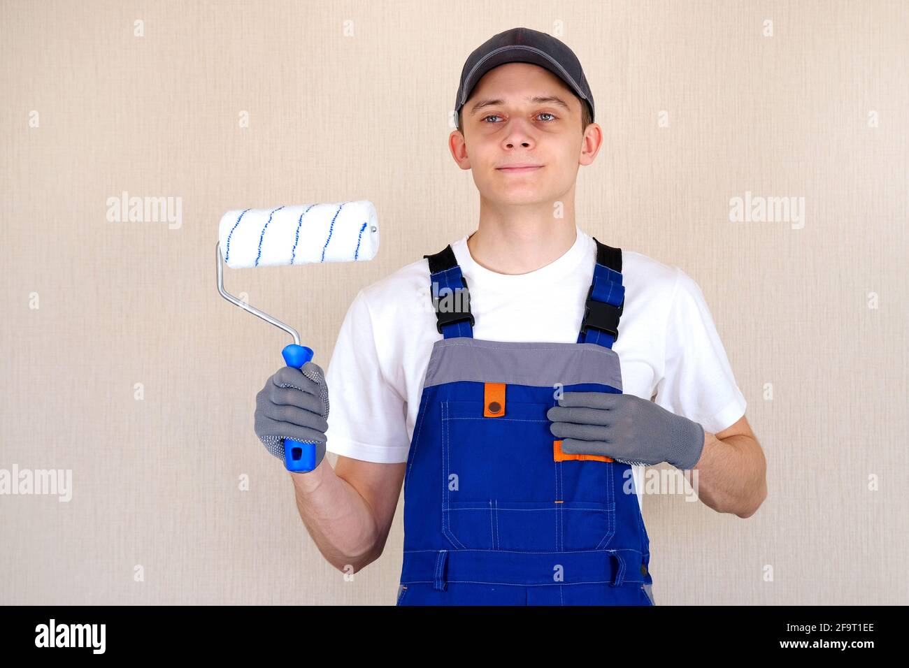 Master painter plasterer in overalls holds a roller in his hand. Blue ...