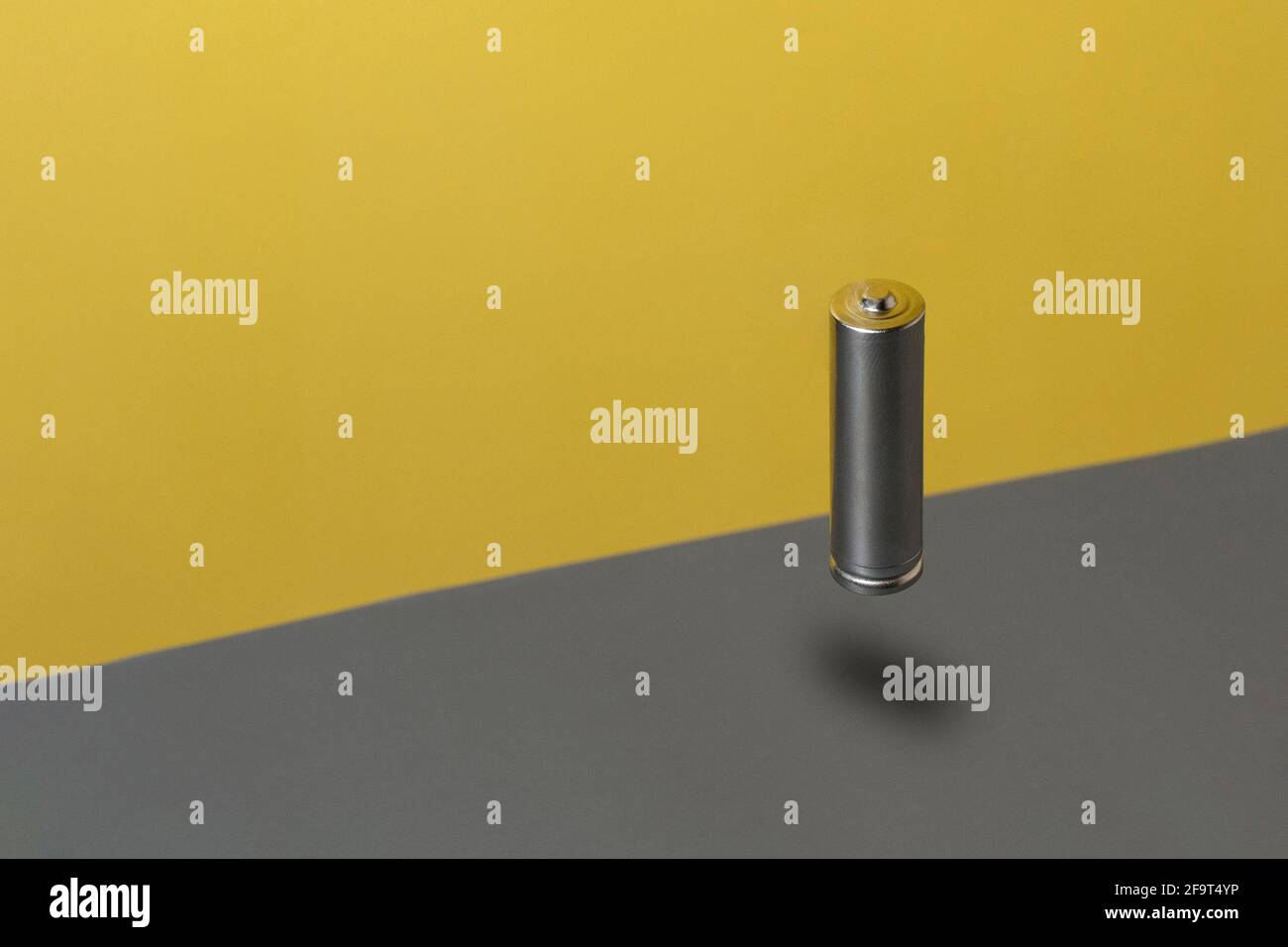Flying alkaline rechargeable battery against grey and yellow background ...