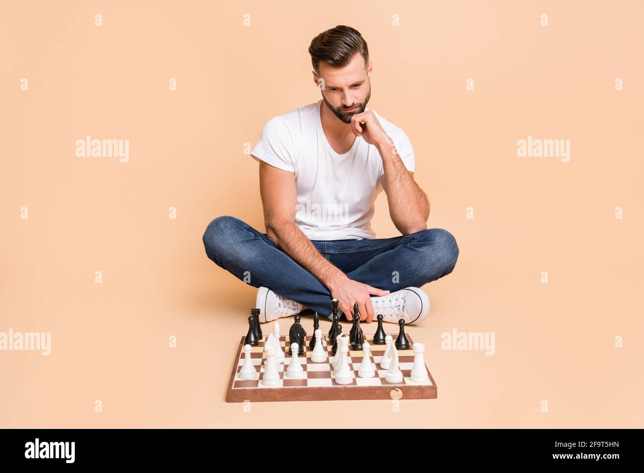 Portrait of nice focused guy sitting on floor playing chess by himself ...