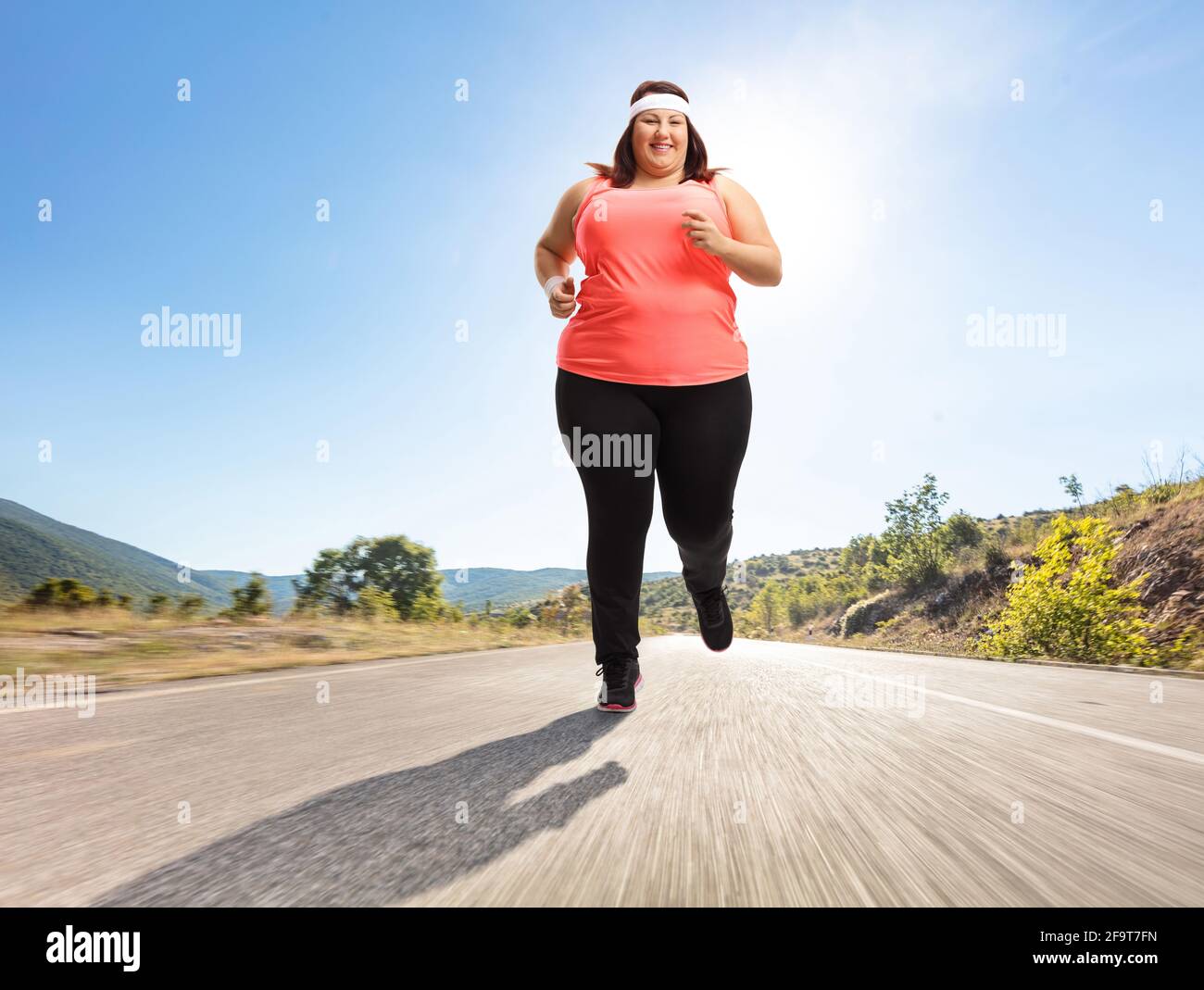 Full length portrait of an overweight woman jogging outdoors on an open ...
