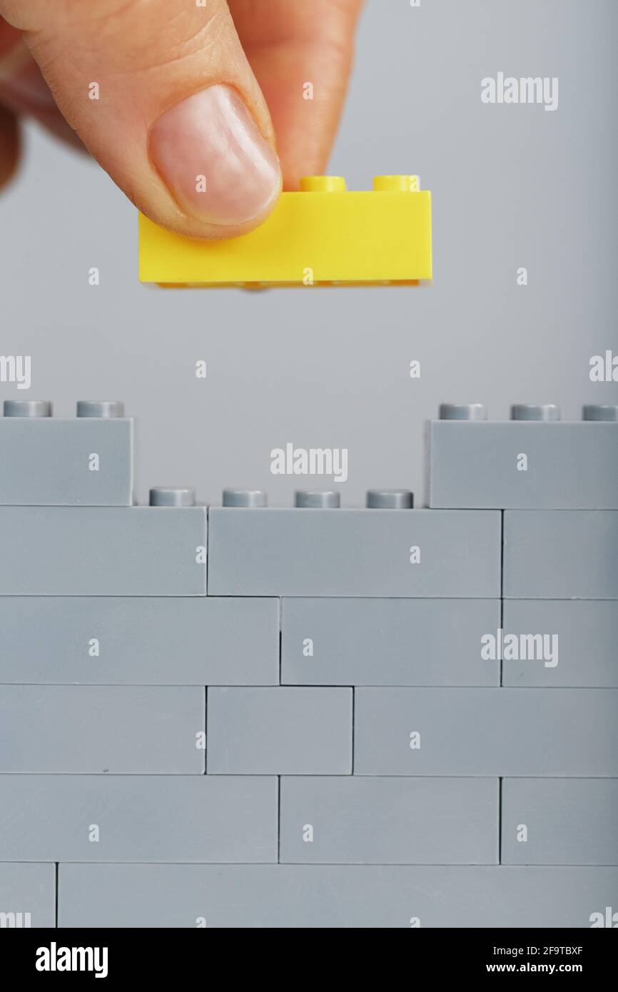 A yellow brick puts a hand on a toy gray wall. The concept of building ...