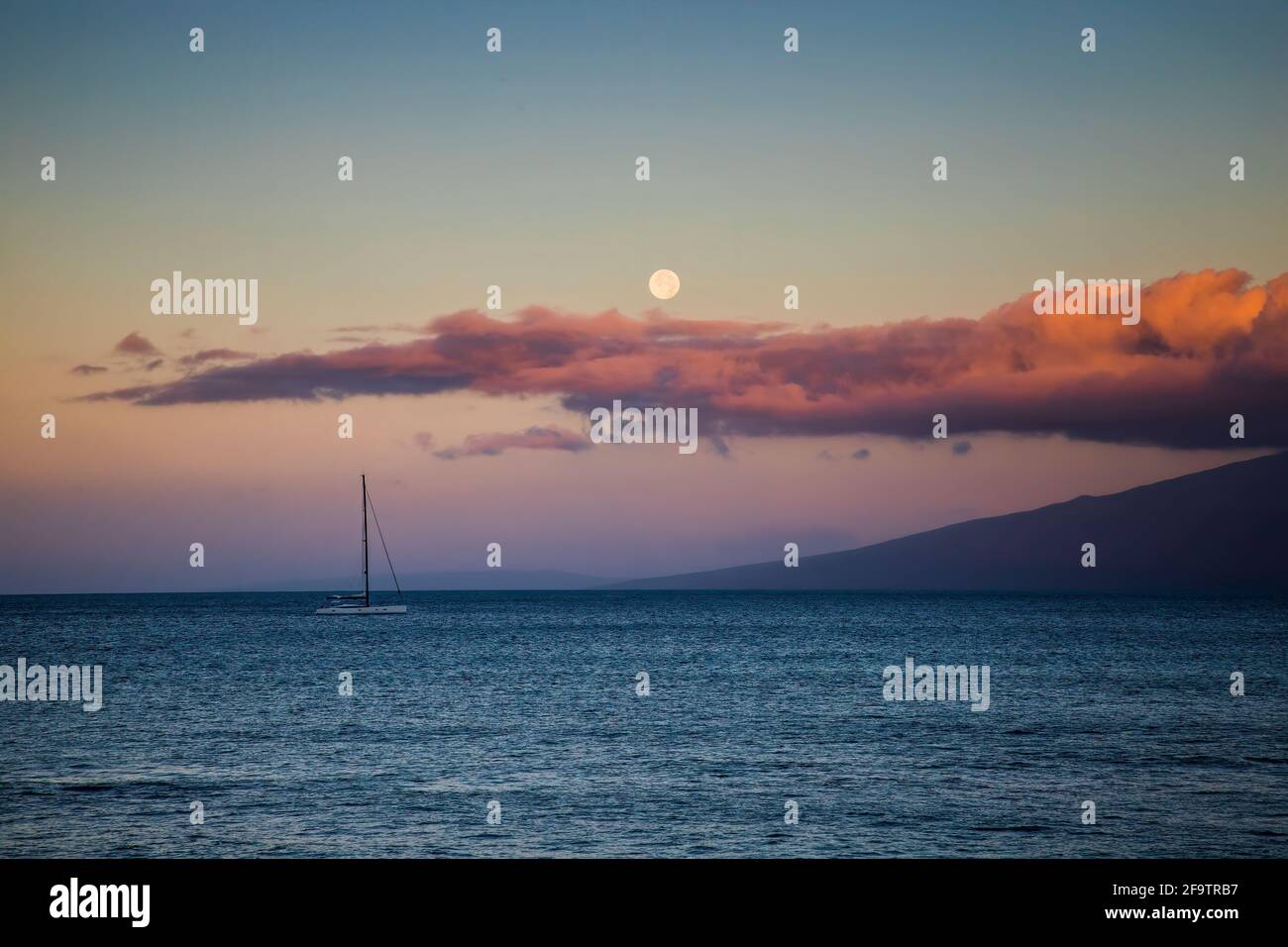 Moon setting as dawn arrives over Pacific ocean with pink clouds and a ...