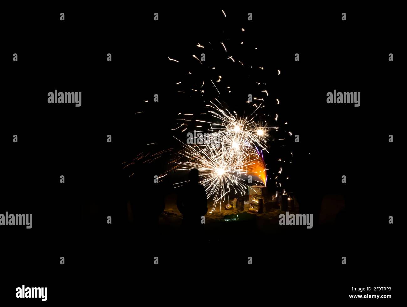 People in silhouette watch a stack of fireworks explode on a beach in ...