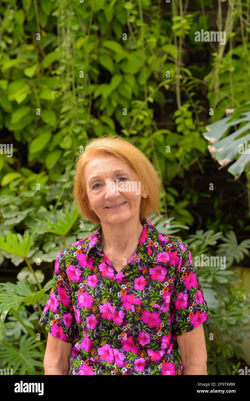 Portrait of a senior woman smiling outdoors at garden during summer ...