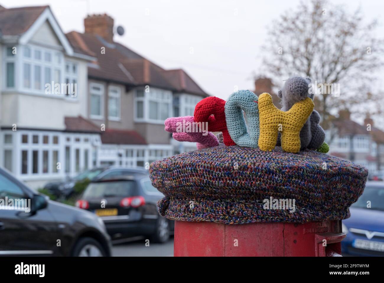 red post box on the street decorated with knitted hat, lettering of ...