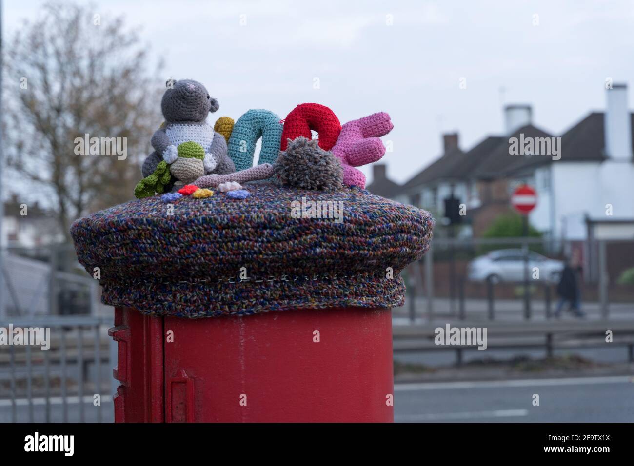 red post box on the street decorated with knitted hat, lettering of ...