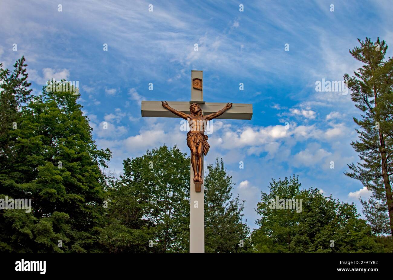 Big white wooden crucifix of Jesus Christ outdoors with trees, blue sky ...