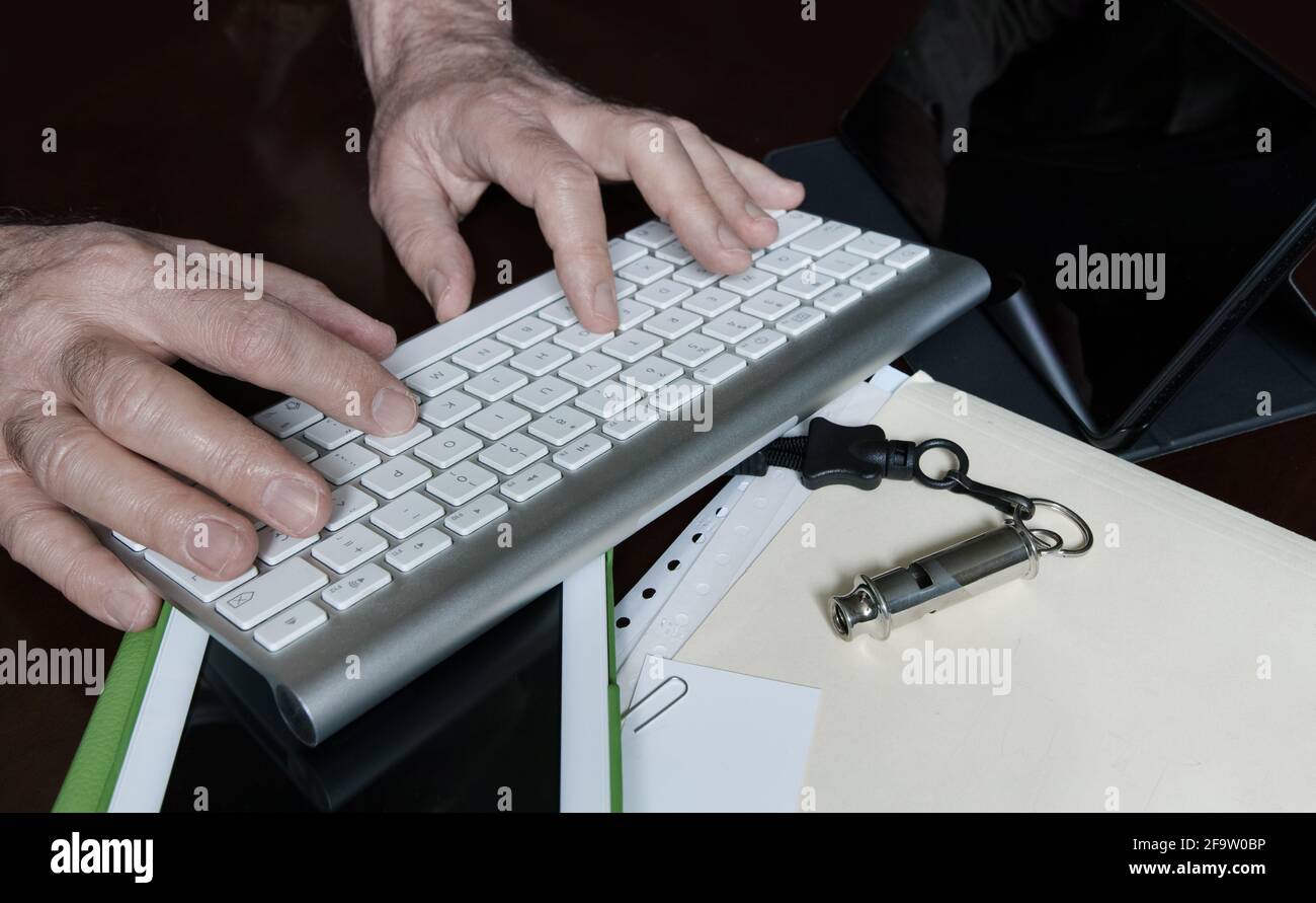 A man's hands on a computer keyboard, documents, and a silver whistle ...
