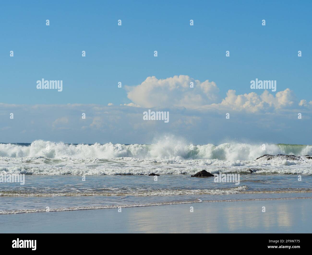Beach with clouds reflected in the water in the wet sand waves breaking ...