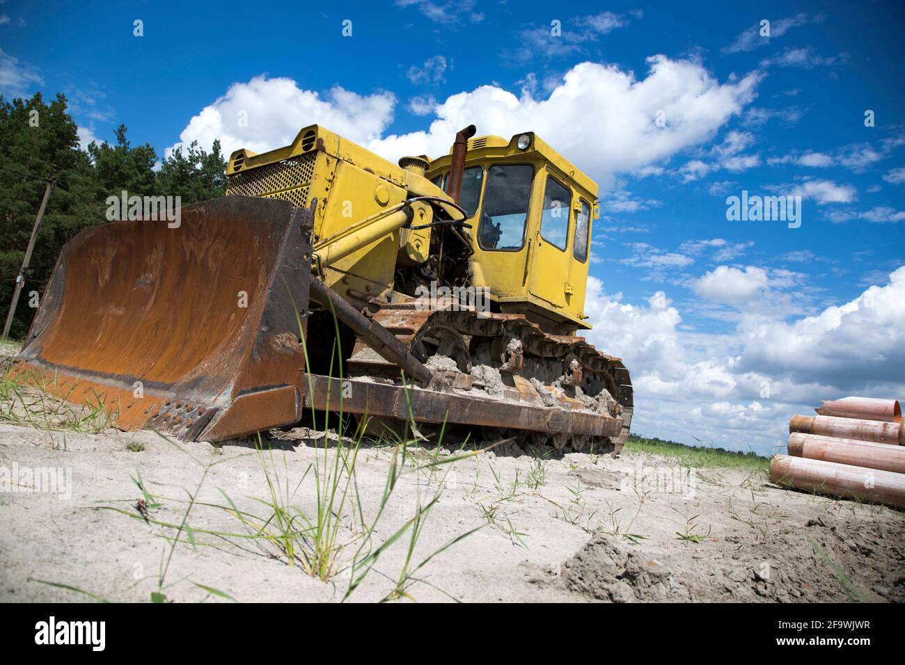 Yellow tractor on the sand on the forest background Stock Photo - Alamy