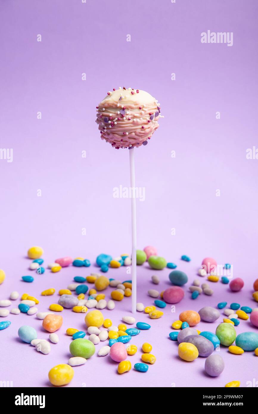 Creamy cake pop over heap of colorful sweets against violet background ...