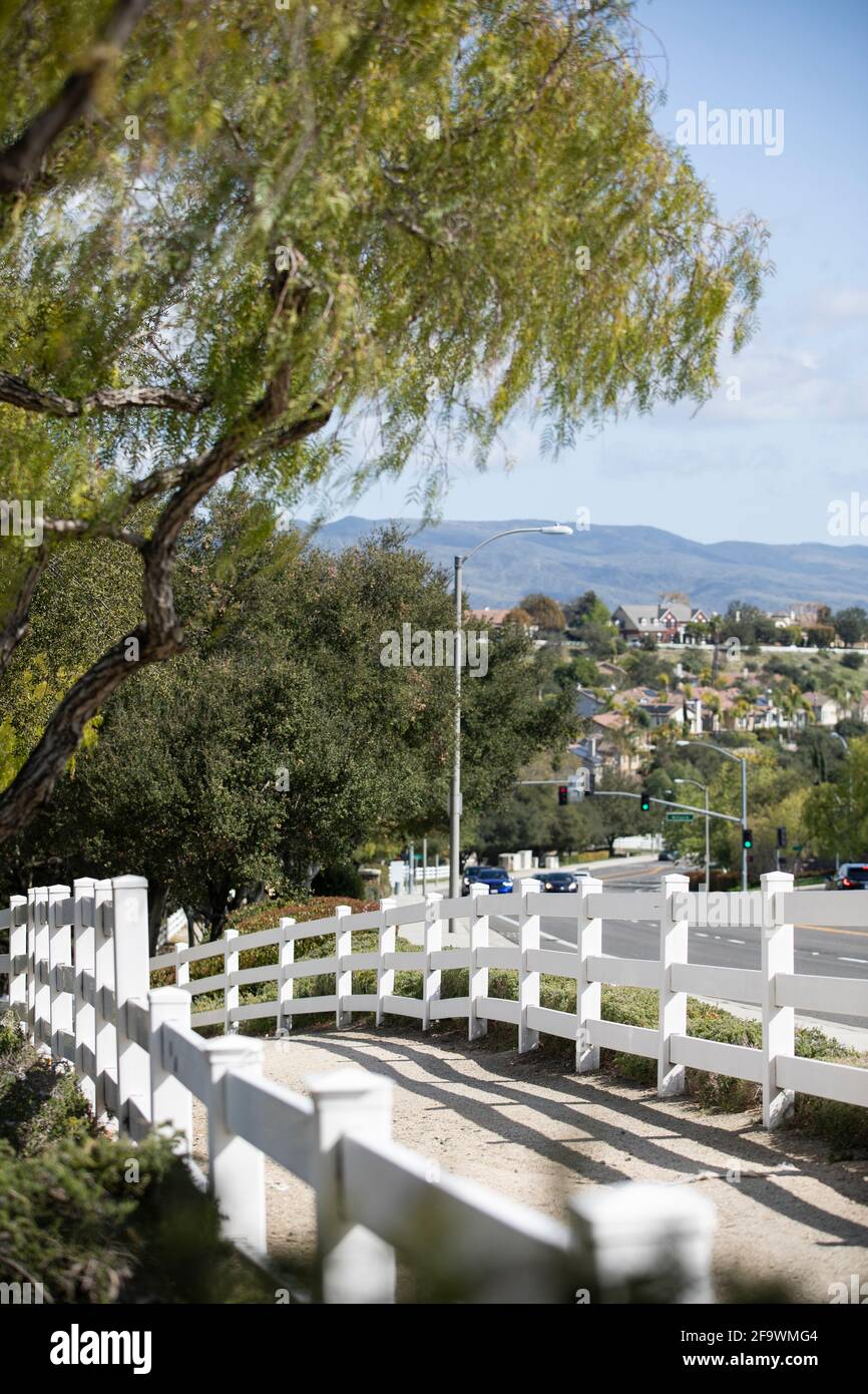 Pepper trees and a white fence frame a public sidewalk in Coto de Caza ...