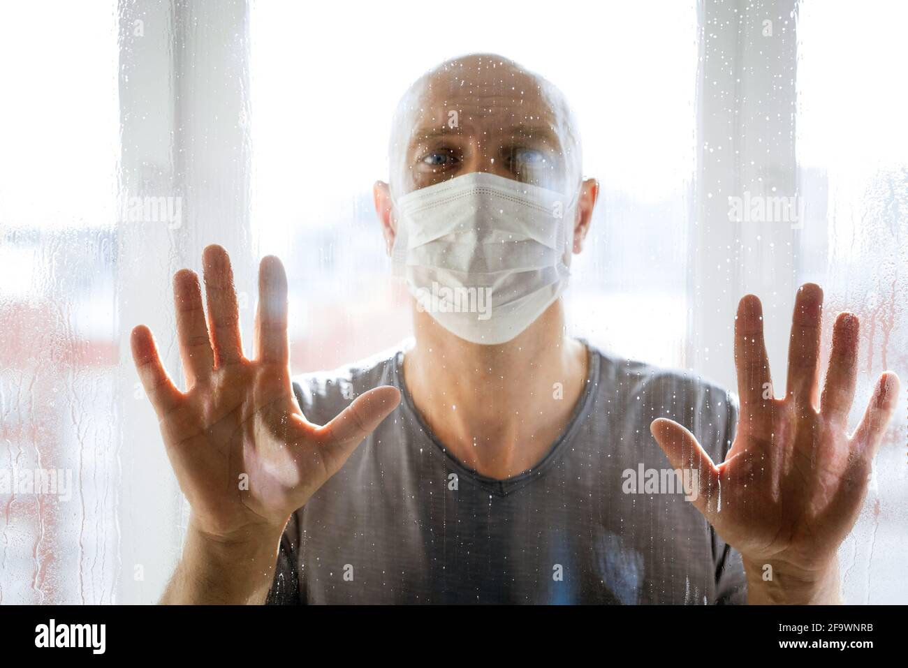 portrait of a bald man in a protective mask looking through the windows ...