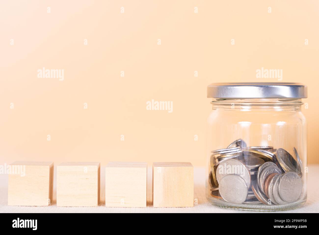 Wooden block and coin inside jar isolated orange background. Saving ...