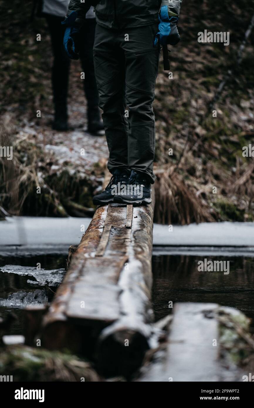 Vertical shot of a young male crossing a river through a wooden board ...