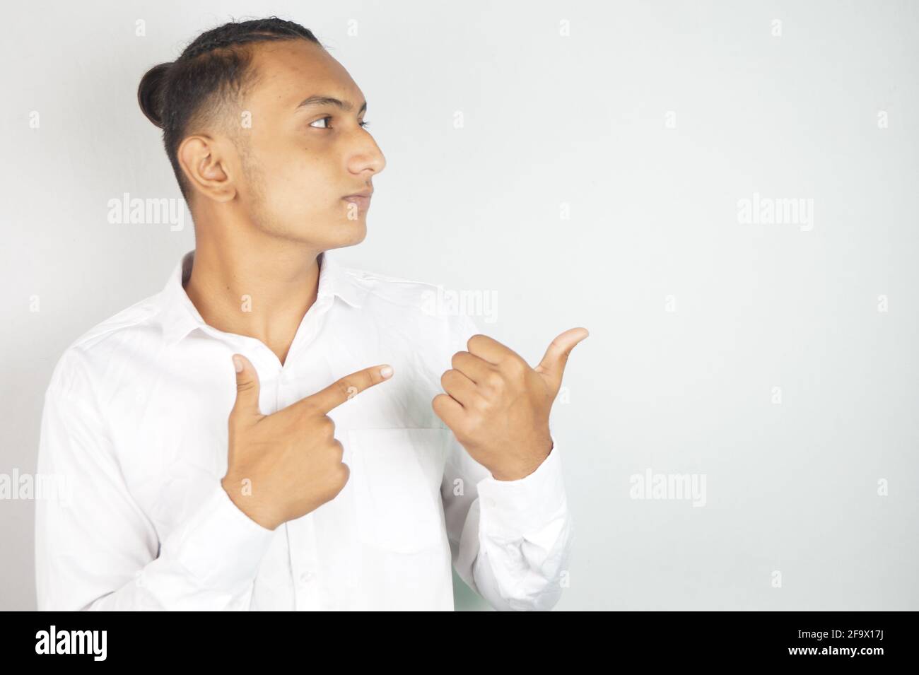 Young South Asian guy wearing a white shirt pointing to the left ...