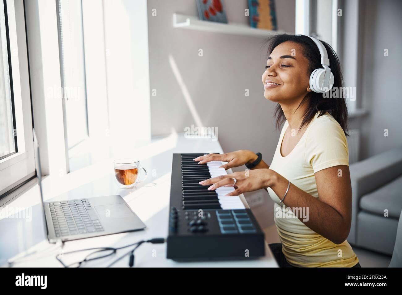 Joyful young woman playing synthesizer and using notebook at home Stock ...