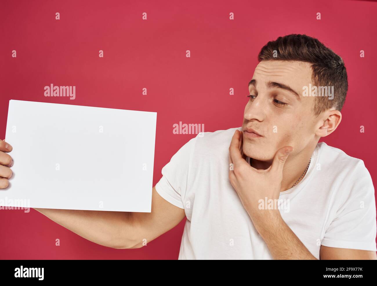 Puzzled young man on a red background are looking at a flyer in hand ...