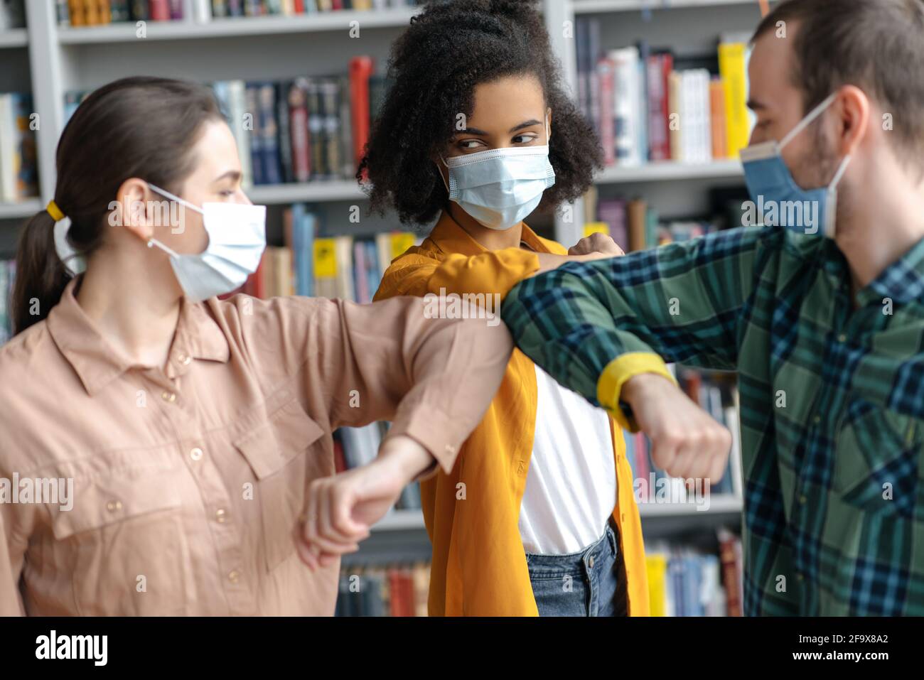 Happy student friends wearing protective face masks greeting bumping ...
