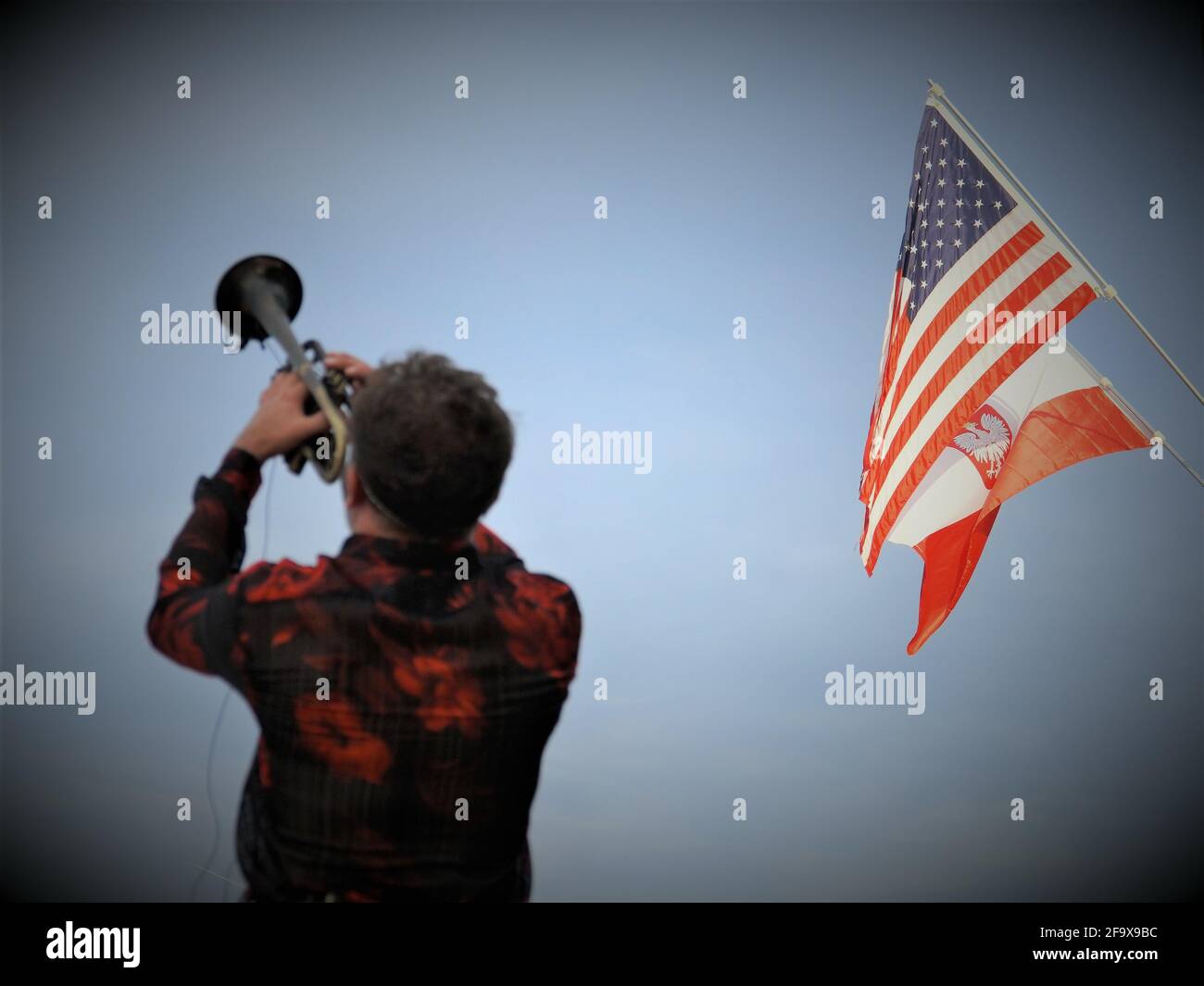 A musician playing trumpet and two flags of Poland and USA in the blue ...