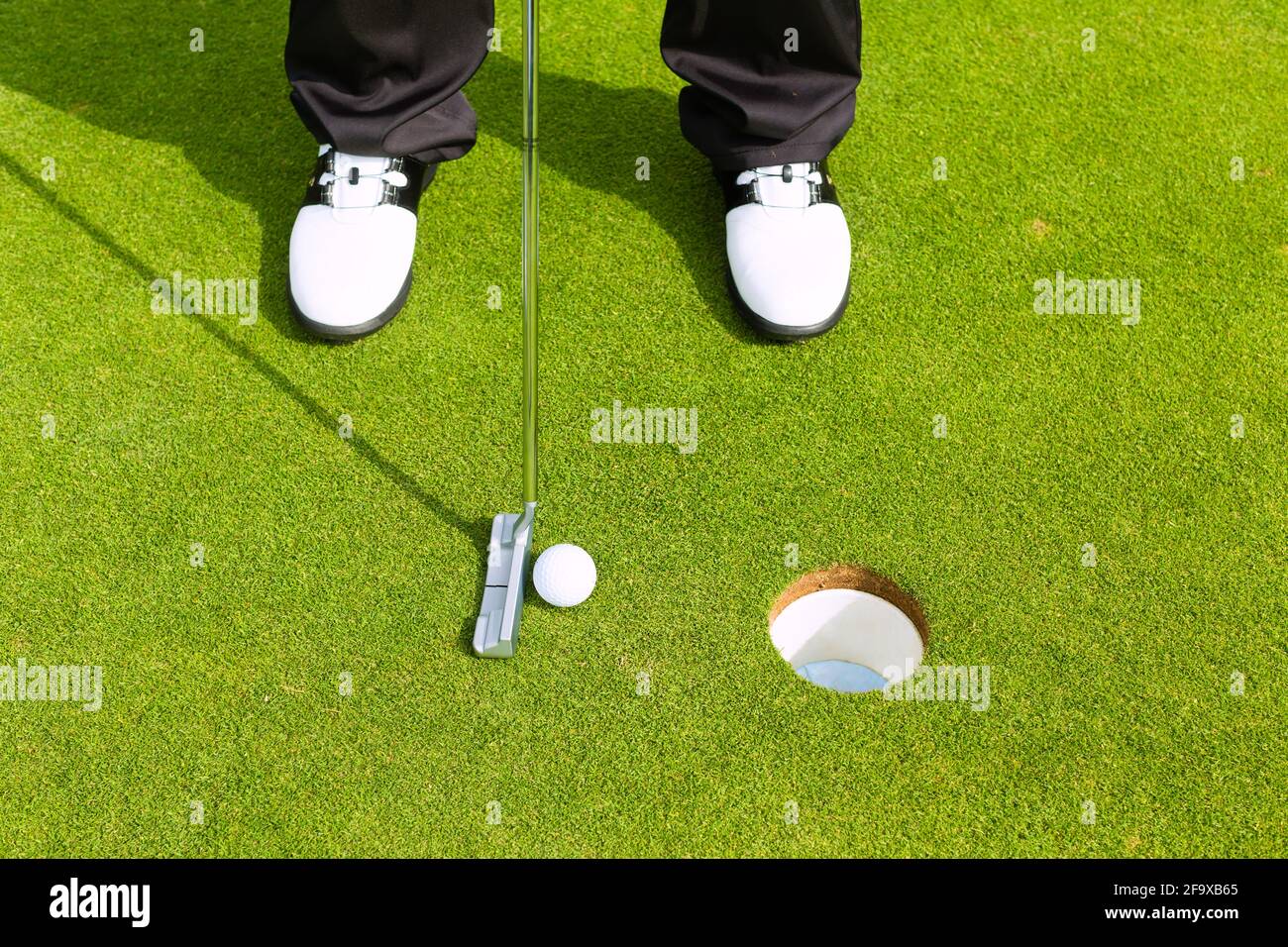 Golf player putting ball into hole, only feet and iron to be seen Stock ...