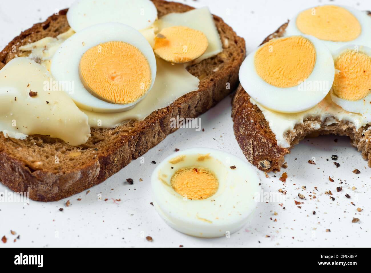 Two sliced bread with butter and cut boiled egg, one of them has a bite ...