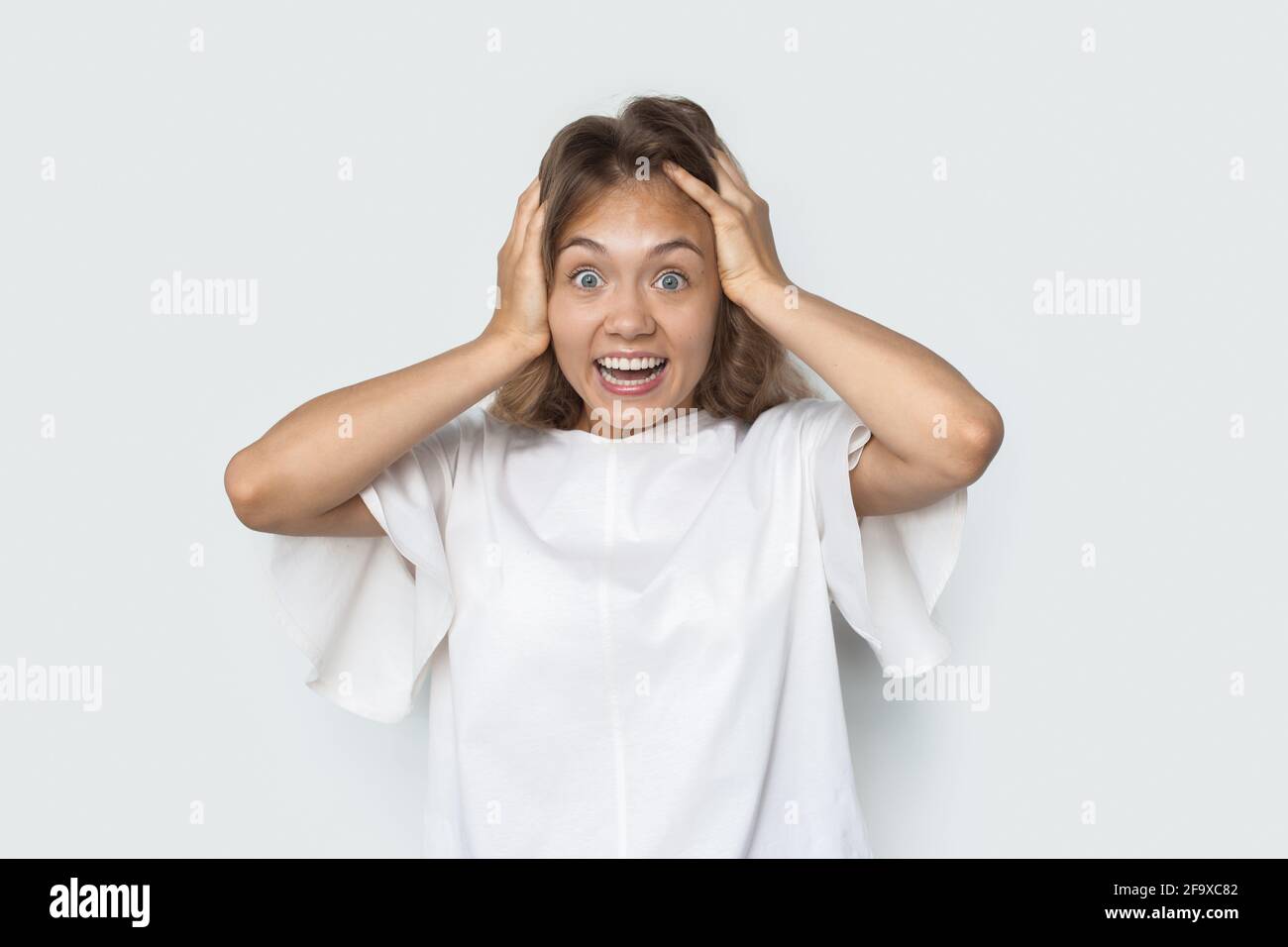 Screaming woman is holding her head and smile at camera on a white ...