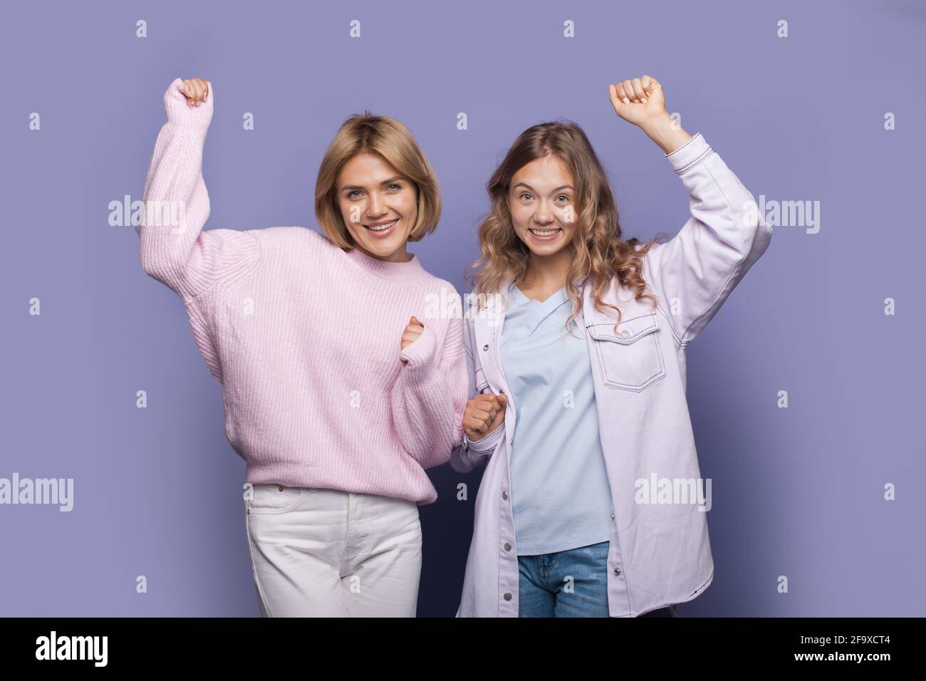Dancing sisters are cheering on a violet studio wall smiling at camera ...