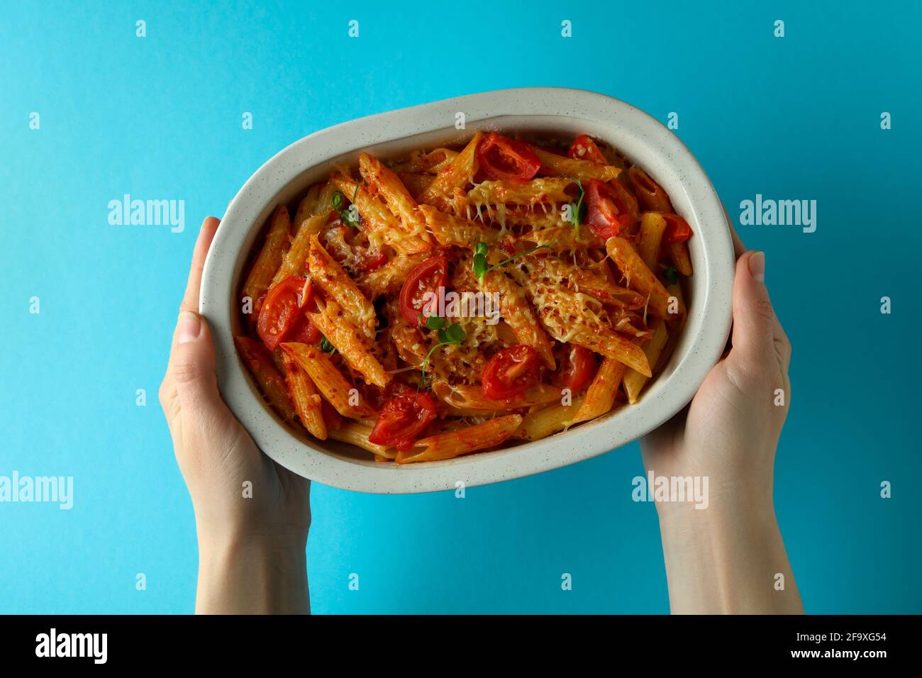 Female hands hold tray with pasta with tomato sauce on blue background ...