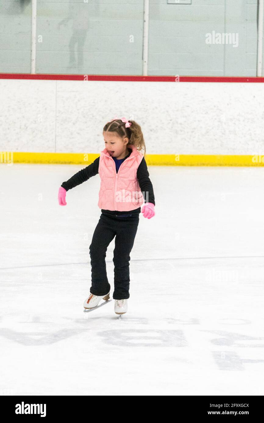 Little girl practicing figure skating moves on the indoor ice rink ...