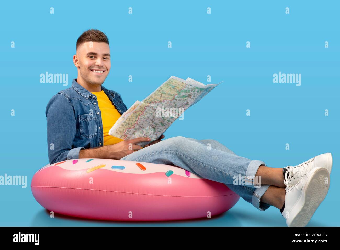 Cool young man sitting on inflatable ring with map, looking at camera ...