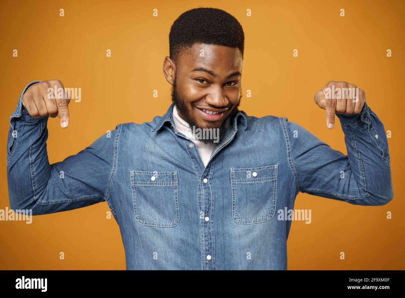 Young african american man pointing down and smiling, yellow background ...