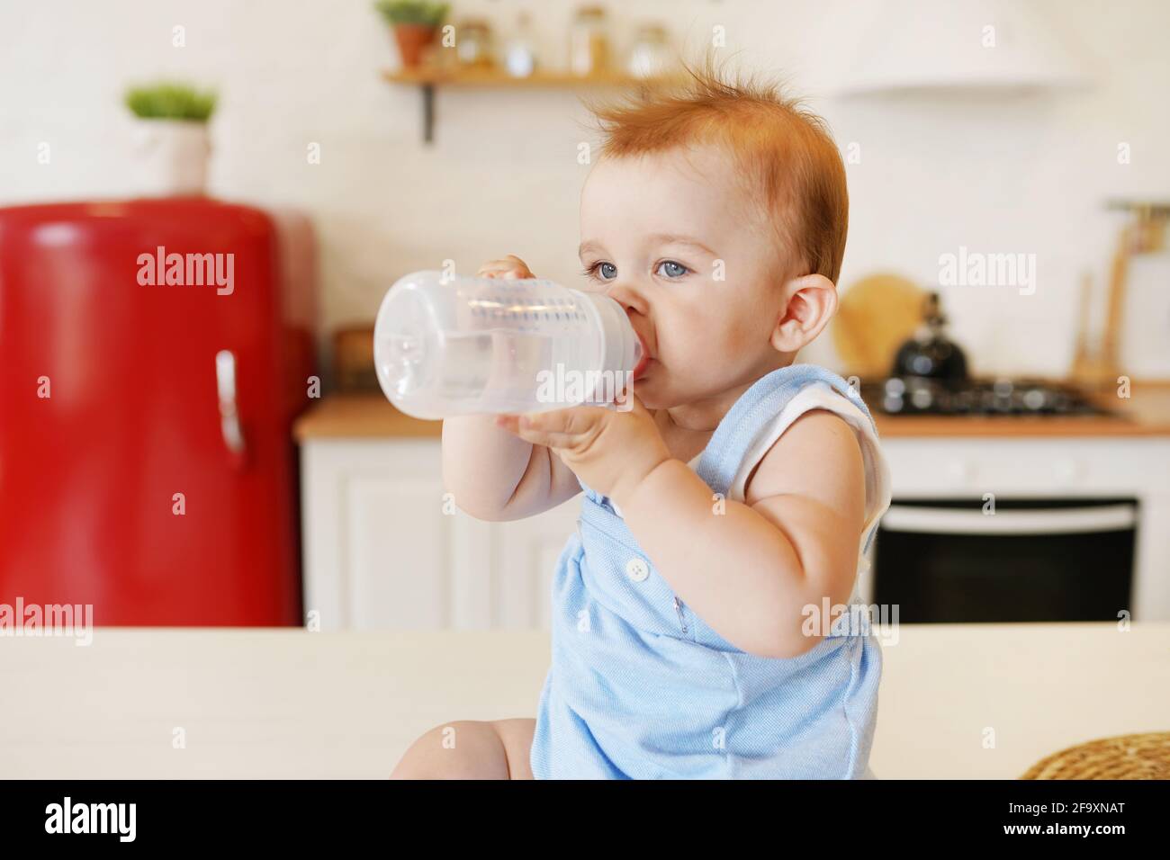 adorable child drinking water from bottle sitting on the table in the ...