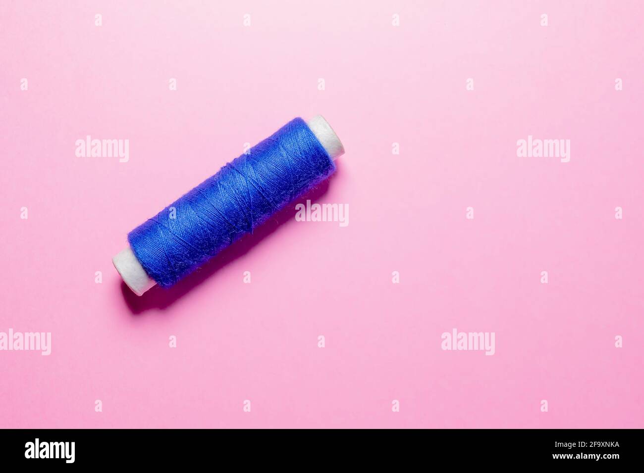 Sewing machine thread reel of blue color on pink background with ...