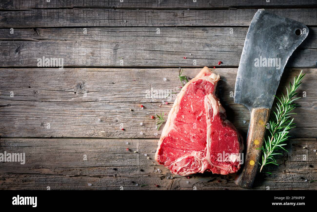 T-bone beef steak - Raw meat for grill with fresh herbs and cleaver ...