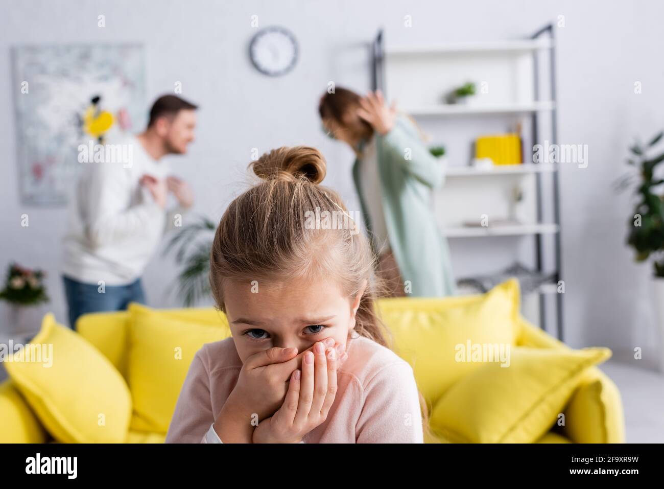 Scared child standing near parents quarrelling in living room on ...