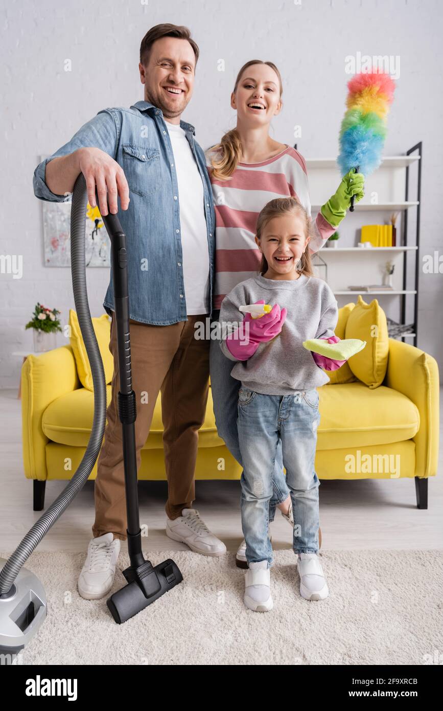 Happy family with detergent, vacuum cleaner and dust brush looking at ...