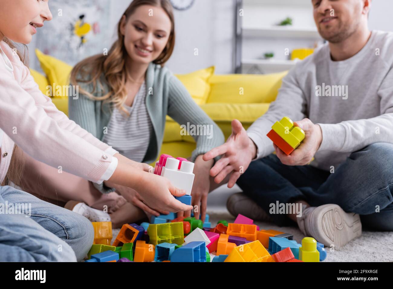 Smiling kid playing building blocks near parents on blurred background ...