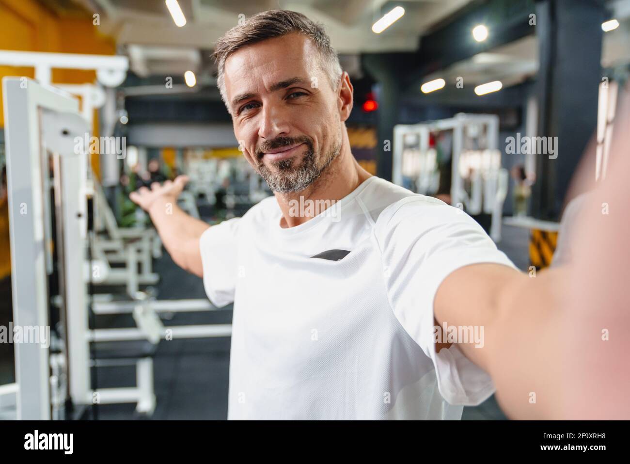 Joyful grey adult sportsman showing copyspace while taking selfie photo ...