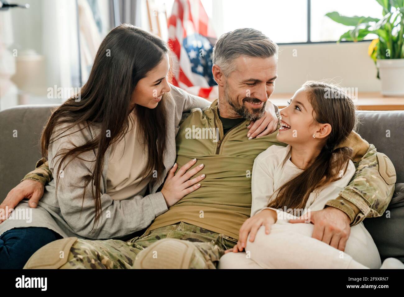 Happy masculine military man hugging his family while sitting on sofa ...