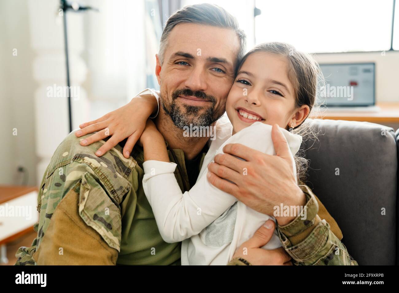 Happy masculine military man hugging his smiling daughter while sitting ...