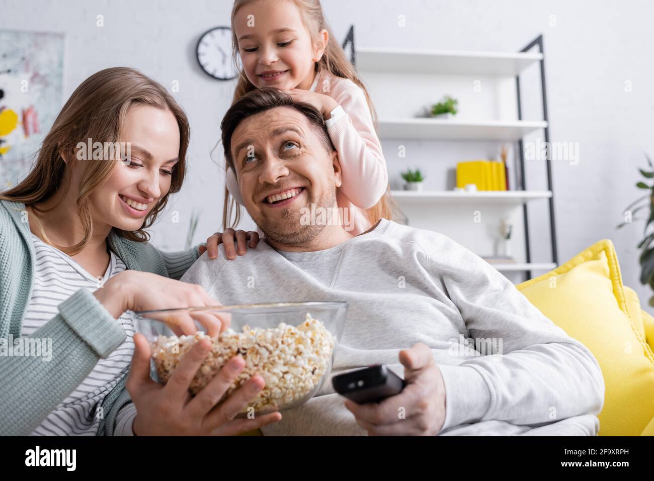 Positive kid looking at parents with popcorn and remote controller ...