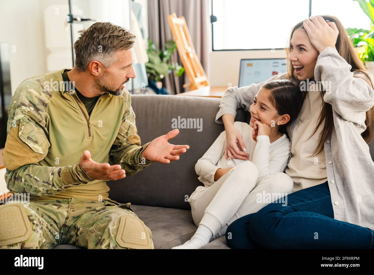 Masculine military man gesturing while talking his happy family indoors ...