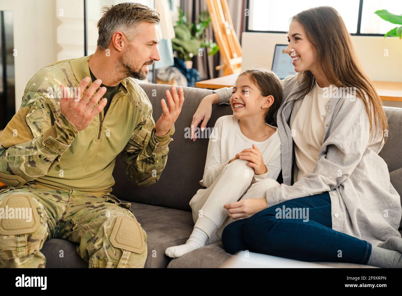 Masculine military man gesturing while talking his happy family indoors ...