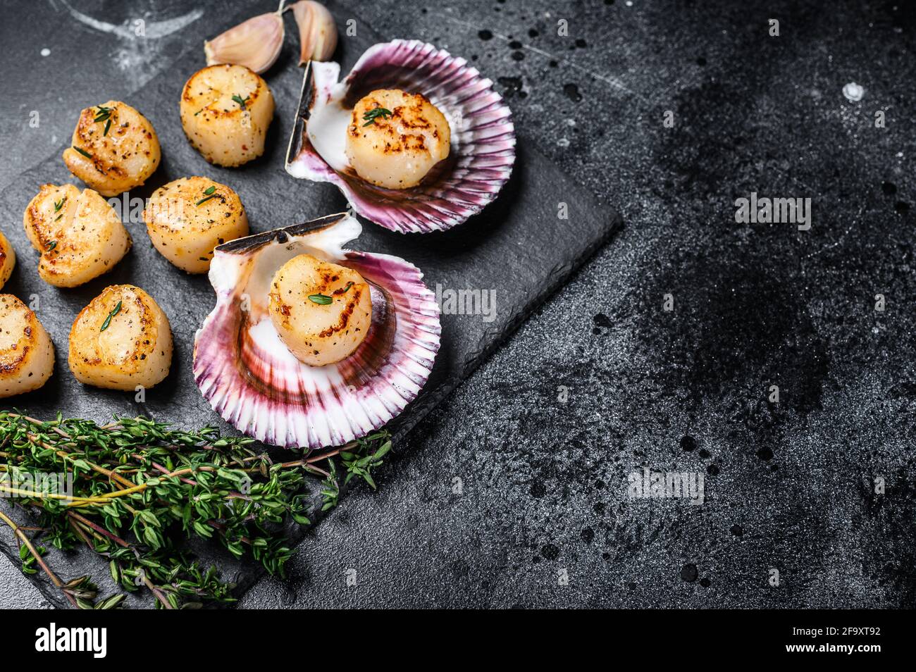 Fried seafood scallops meat with butter in a shells. Black background ...