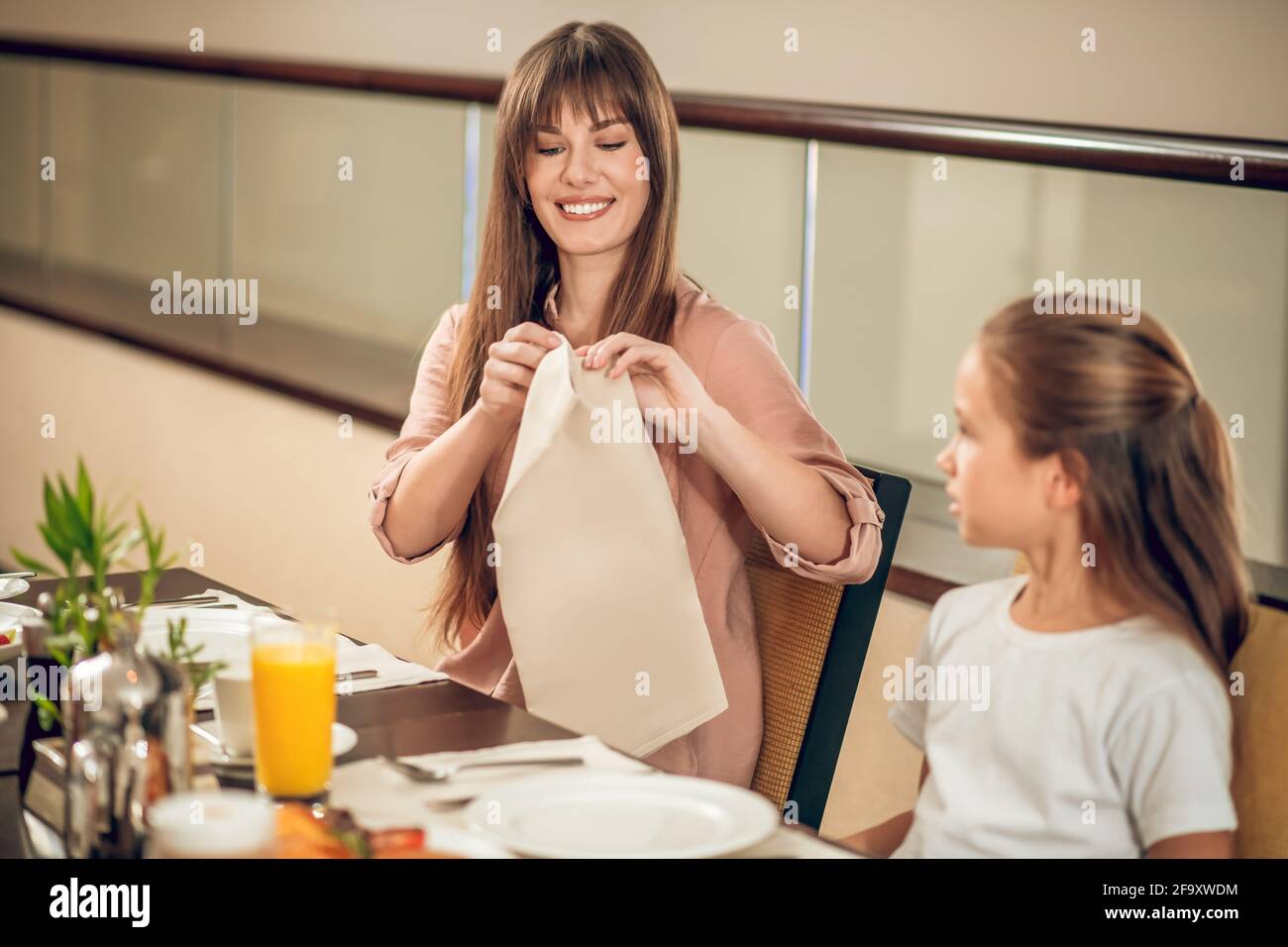 Mom opening a napkin to cover her daughter during breakfast Stock Photo ...