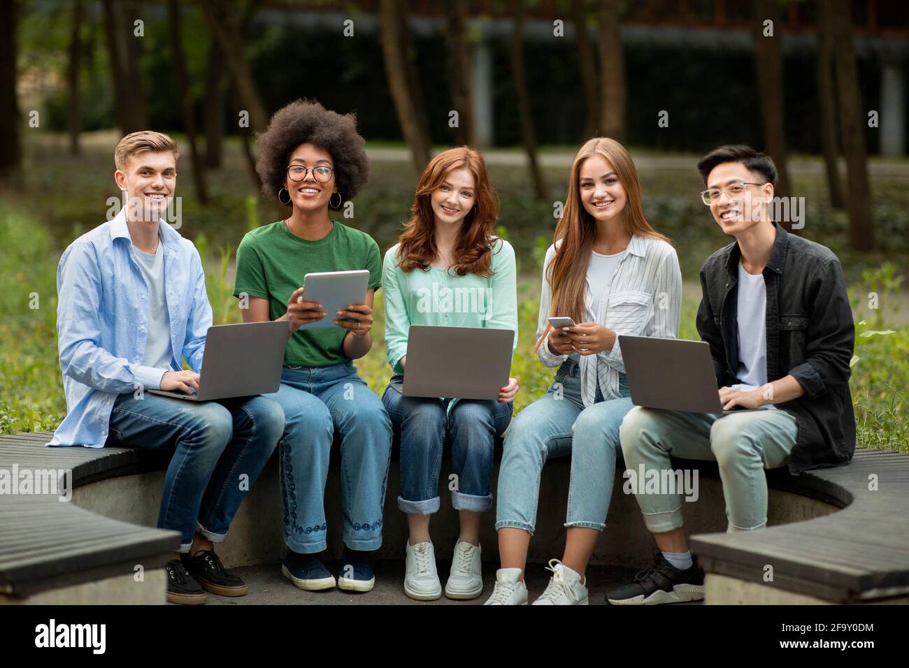 Best gadgets for students. Multiracial teens sitting with electronic ...